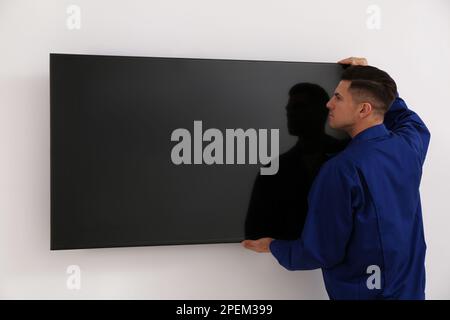 Professional technician installing modern flat screen TV on wall ...