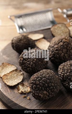 Whole and cut truffles on wooden table against black background ...
