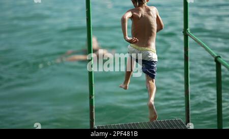 Kid plunging into lake water. Child having fun running by dock and ...
