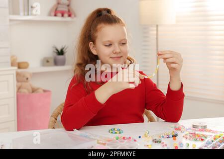 Cute girl making beaded jewelry at table in room Stock Photo - Alamy
