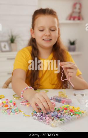 Cute girl making beaded jewelry at table in room Stock Photo - Alamy