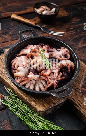 Fried baby octopuses in a skillet with herbs. Wooden background. Top ...