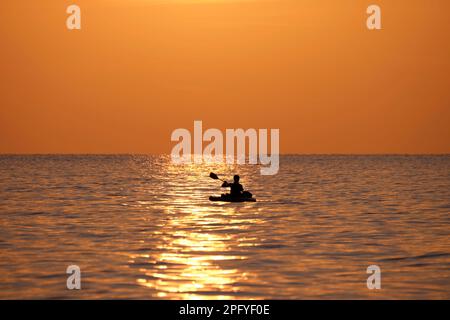 Dark figure of sportsman rowing alone on his kayak boat on sea water at ...