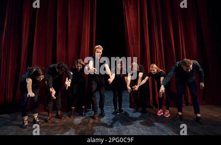 People bowing to audience. Group of actors in dark colored clothes on ...