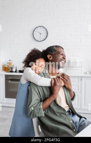 Black preteen girl with curly hair smiling and using cellphone isolated ...
