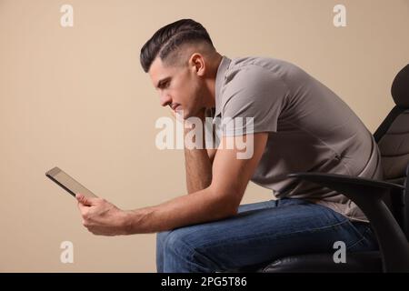 Man with poor posture using tablet while sitting on chair against beige ...