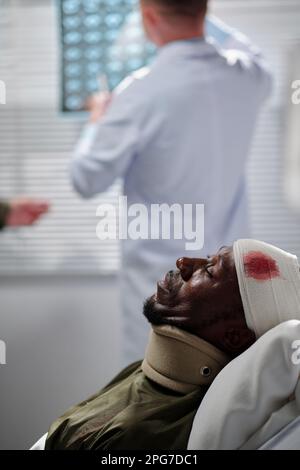 Wounded African American patient with injured head lying on bed in ward ...