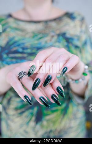 Woman's hand with long nails and green manicure with bottles of nail ...