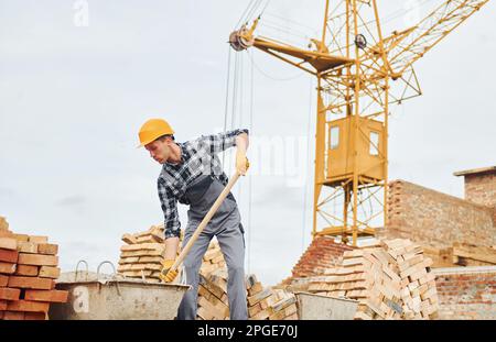 Using shovel with wooden holder. Construction worker in uniform and ...