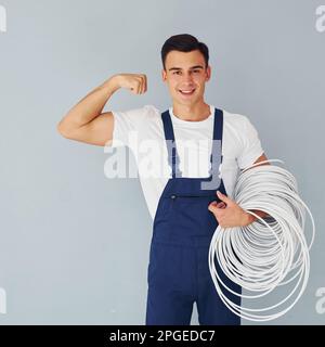 Holds cable. Male worker in blue uniform standing inside of studio ...