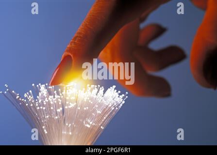 WOMANS INDEX FINGER TIP TOUCHES LIT TIPS OF FIBER OPTIC STRANDS (©KECK ...