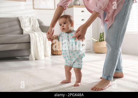 Mother supporting her baby daughter while she learning to walk at home ...