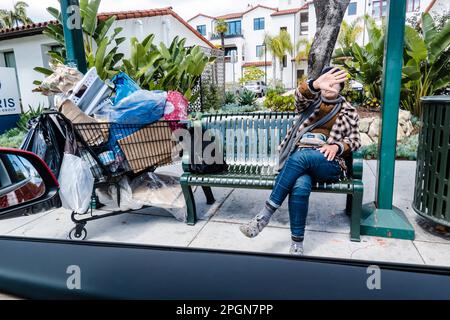 A homeless male sits on a bus stop bench with worldly possessions in a ...