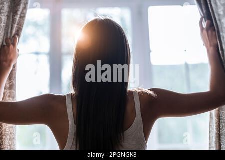 Woman opening window curtains at home in morning, back view Stock Photo ...