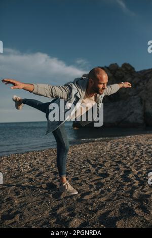 A man balancing on one leg on the rocks and his reflection in a pond of ...