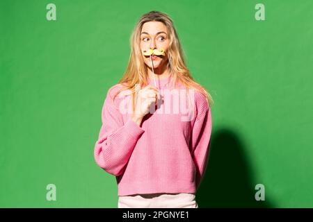 Blond woman imitating mustache standing against green background Stock ...