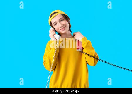 Cool teenage boy with phone receiver showing "call me" gesture on blue ...
