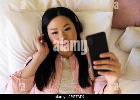 Asian woman wearing headphones using digital tablet on sofa for remote ...