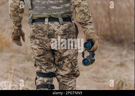 a soldier in camouflage holds binoculars. military man holding ...