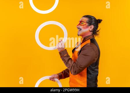 A cheerful circus performer skillfully juggling a number of clubs ...