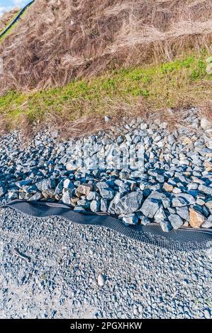 A hillside with growth and brush, with a rock layer for drainage, and a ...