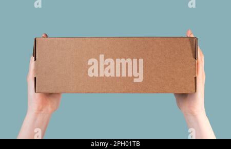 A hand holding a brown kraft cardboard box. Craft paper package of rectangular shape, mockup ...