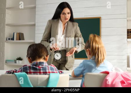 Teacher with alarm clock scolding pupils for being late in classroom ...