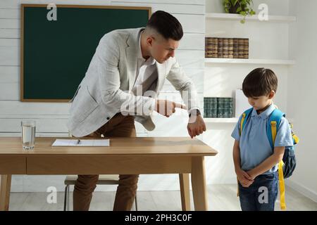 Teacher pointing on wrist watch while scolding pupil for being late in ...