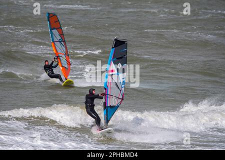 Two windsurfers in black wetsuits entering the water to practise ...