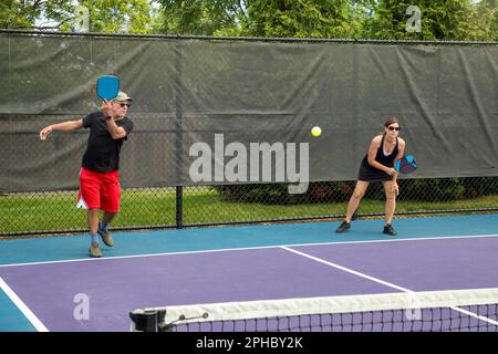 A pickleball player serves while her partner prepares for a return on a ...