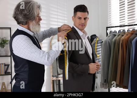 Professional tailor measuring shoulder seam length on client's jacket ...