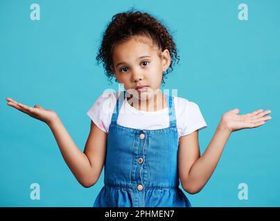 Kids, doubt and a confused girl shrugging her shoulders on a green screen background in studio ...