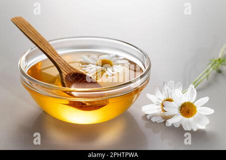 Chamomile syrup in a small bowl and in a jar and chamomile flowers on a ...