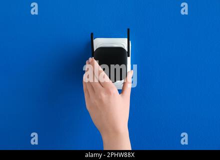 Woman plugging black WiFi repeater in electric socket on white brick ...