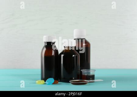 Bottles of syrup, measuring cup, lozenges and spoon on white wooden ...