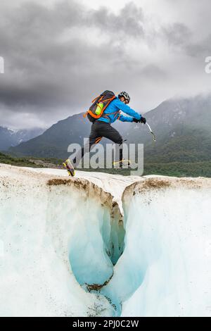 A hiker jumps over a crevasse on a glacier high in the Canadian Rockies ...