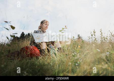 Woman with backpack having break during trip in mountains taking map ...
