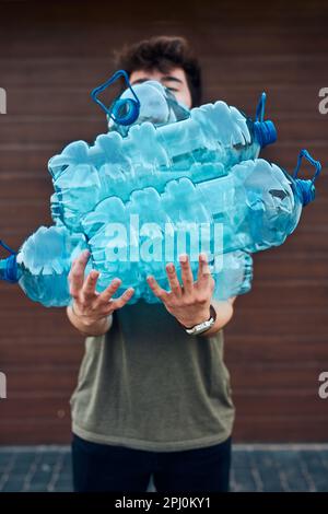 Young man throwing out empty used plastic water bottles into trash bin ...