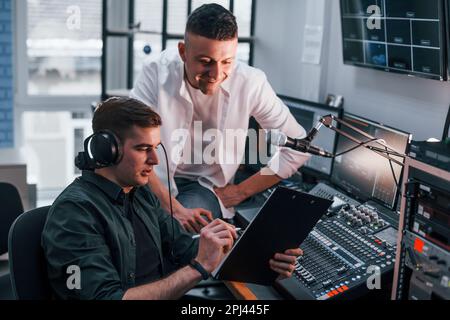 Conception of teamwork. Two guys is indoors in the radio studio is busy ...