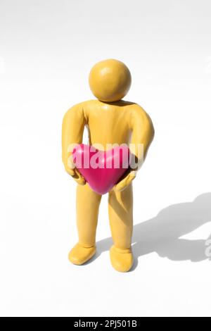 Yellow plasticine human figure with pink heart sitting on book against ...