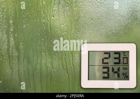 Digital hygrometer with thermometer on glass with water drops. Space ...