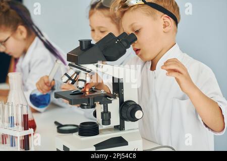 Using microscope. Children in white coats plays a scientists in lab by ...