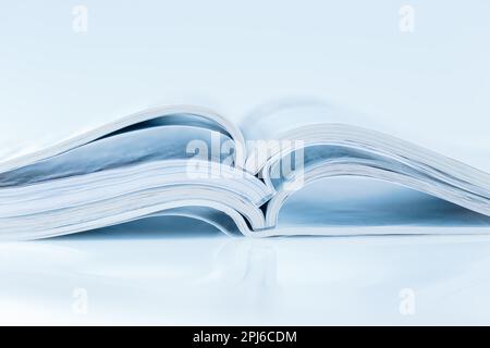 Stack of open magazines in blue tone on white background with copy ...