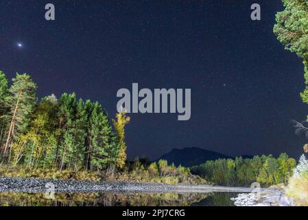 Sirius star over an illuminated river with a stone bank reflection of ...
