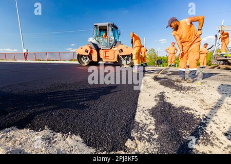 Worker are using rake to level, set up layer of fresh tarmac to right ...