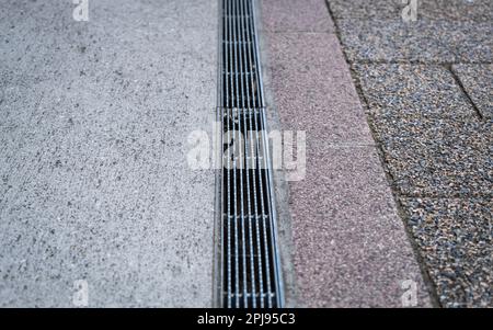 Stainless steel grated flood water storm drain on a Tokyo sidewalk ...