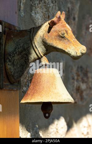 Rustic cow-shaped bell mounted on a wooden wall at a rural farmhouse ...