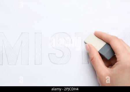 Woman erasing word on sheet of white paper at wooden table, top view ...