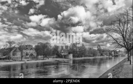 A river flows towards a historic iron bridge with a cloud filled sky ...