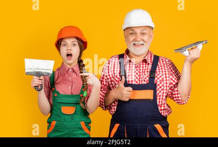 happy child and grandfather plasterer in helmet on yellow background ...
